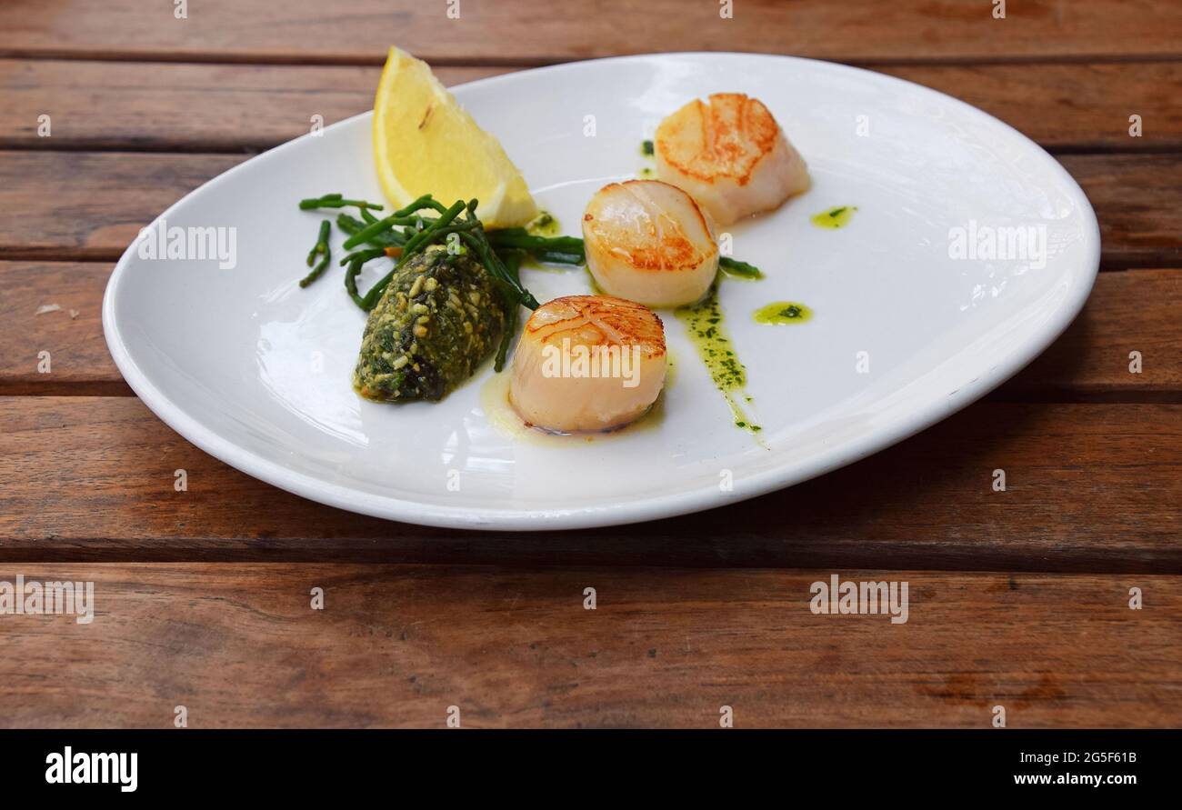 Close up portion of three grilled scallops on white plate over brown ...