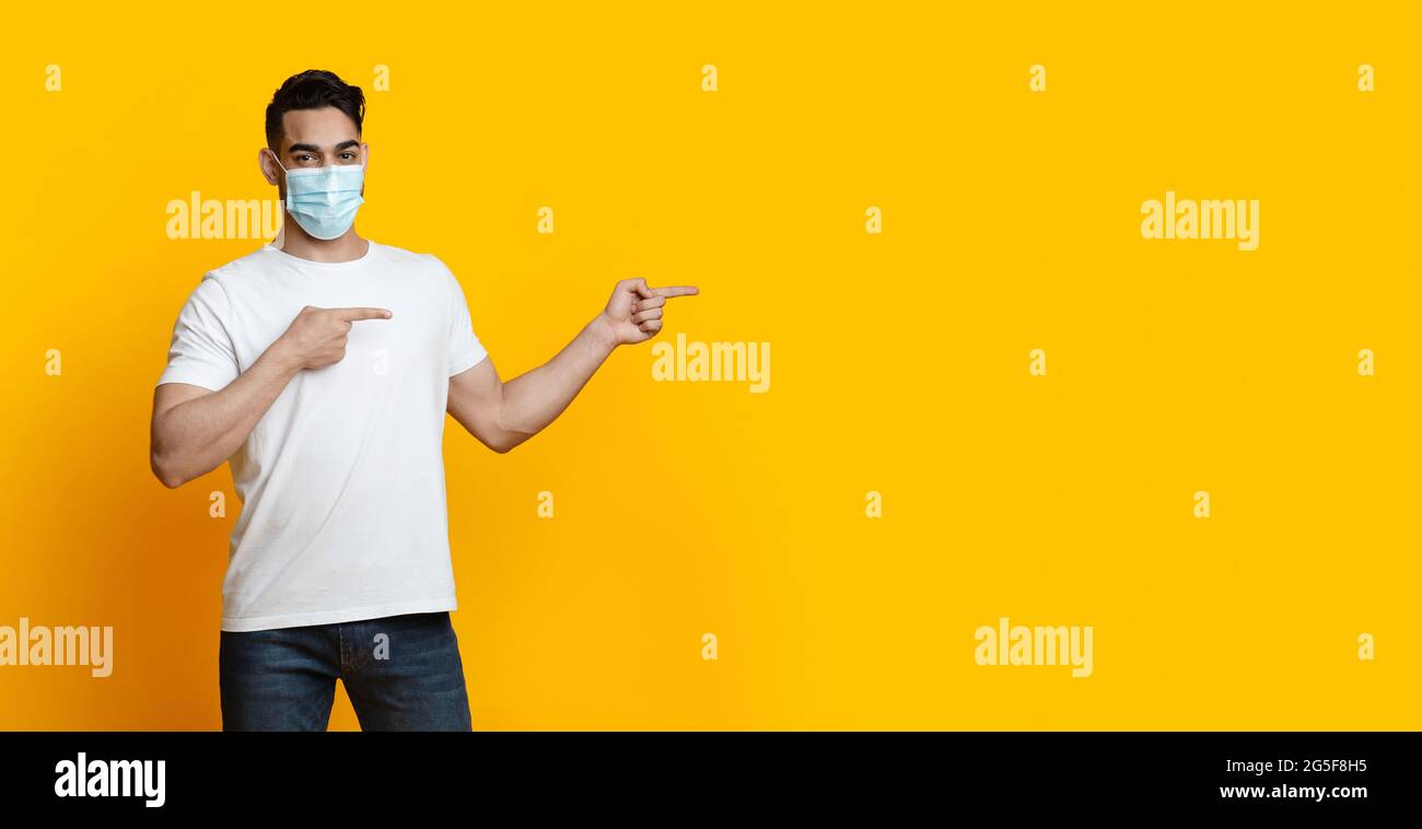 Arab guy in protective face mask pointing at copy space for text or ...