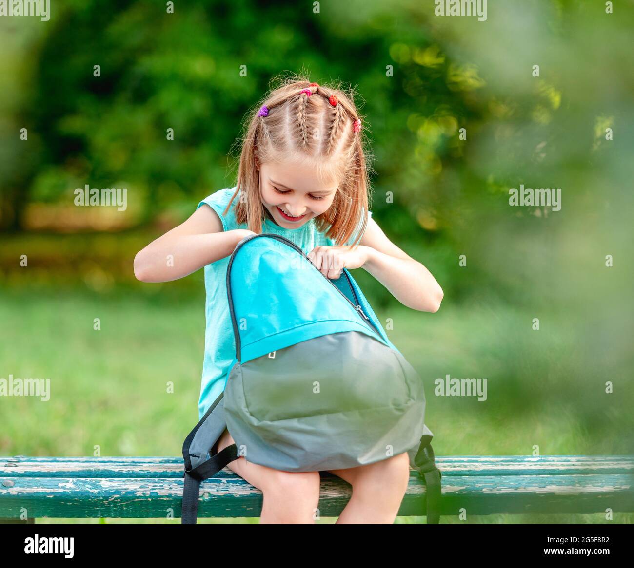 Schoolgirl peeking into backpack in park Stock Photo - Alamy