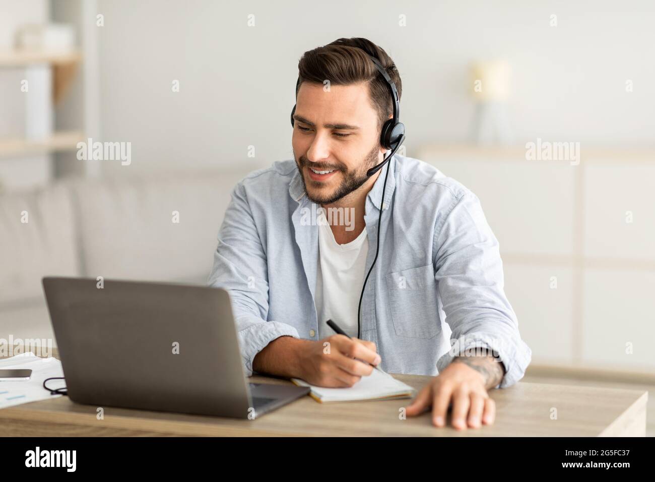 New knowledge online at home. Young man in headphones making notes and ...