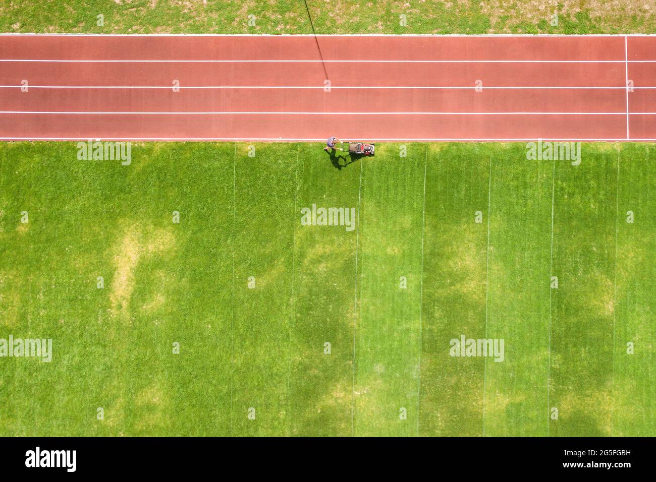 Aerial view of small figure of worker cutting green grass with mowing ...
