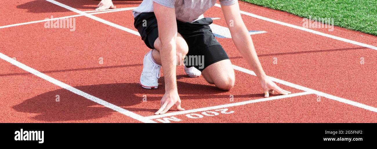 A high school boy is on his mark at the 200 meter start line on a red ...