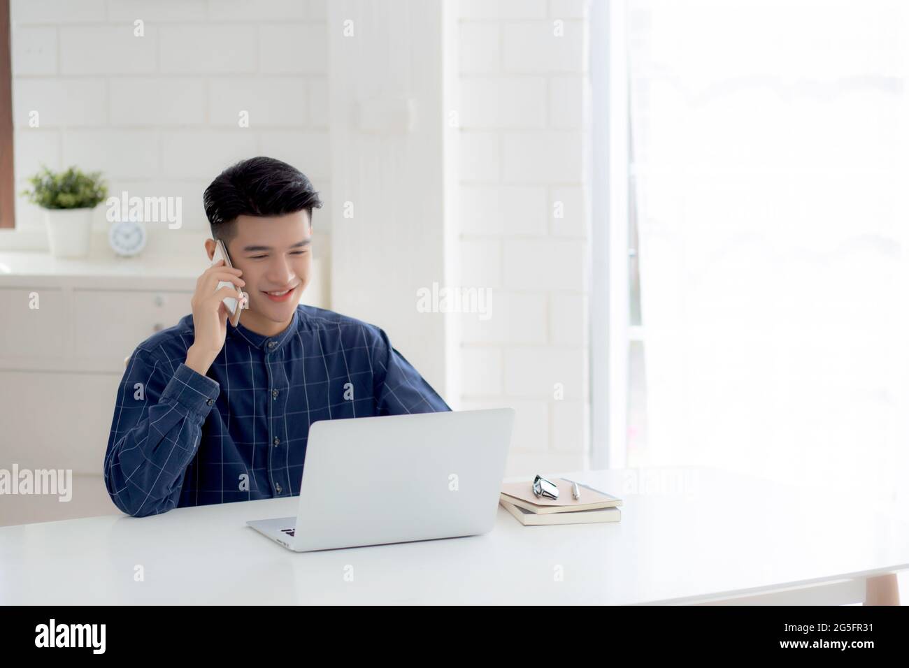 Young asian man talking phone and work from home with laptop computer ...
