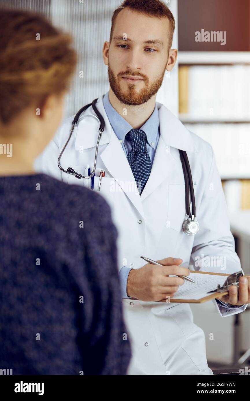 Friendly bearded doctor and patient woman discussing current health ...