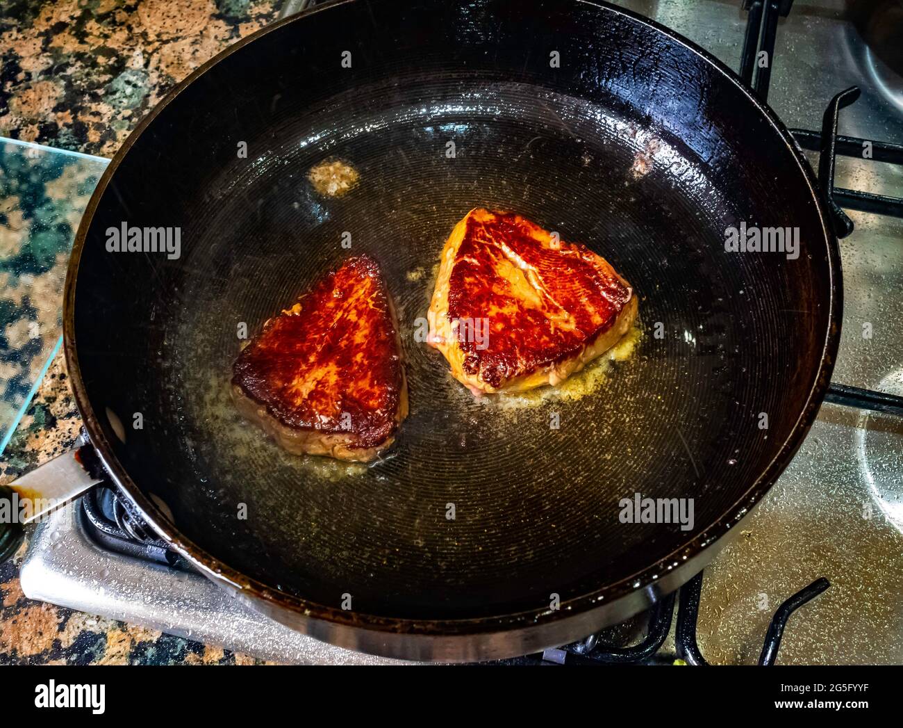 The second side of two small fillet beef steaks being fried in olive ...