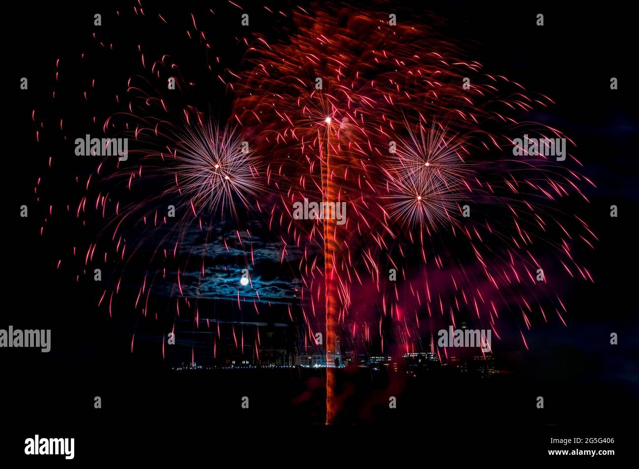 Red fireworks fill the night sky, raining down sparks of color over ...