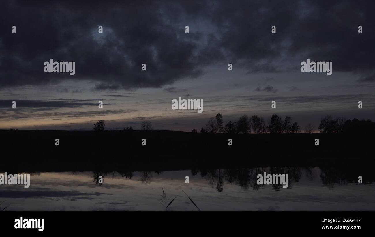 Nightfall time panorama at the lake with a dark cloudy sky reflecting ...