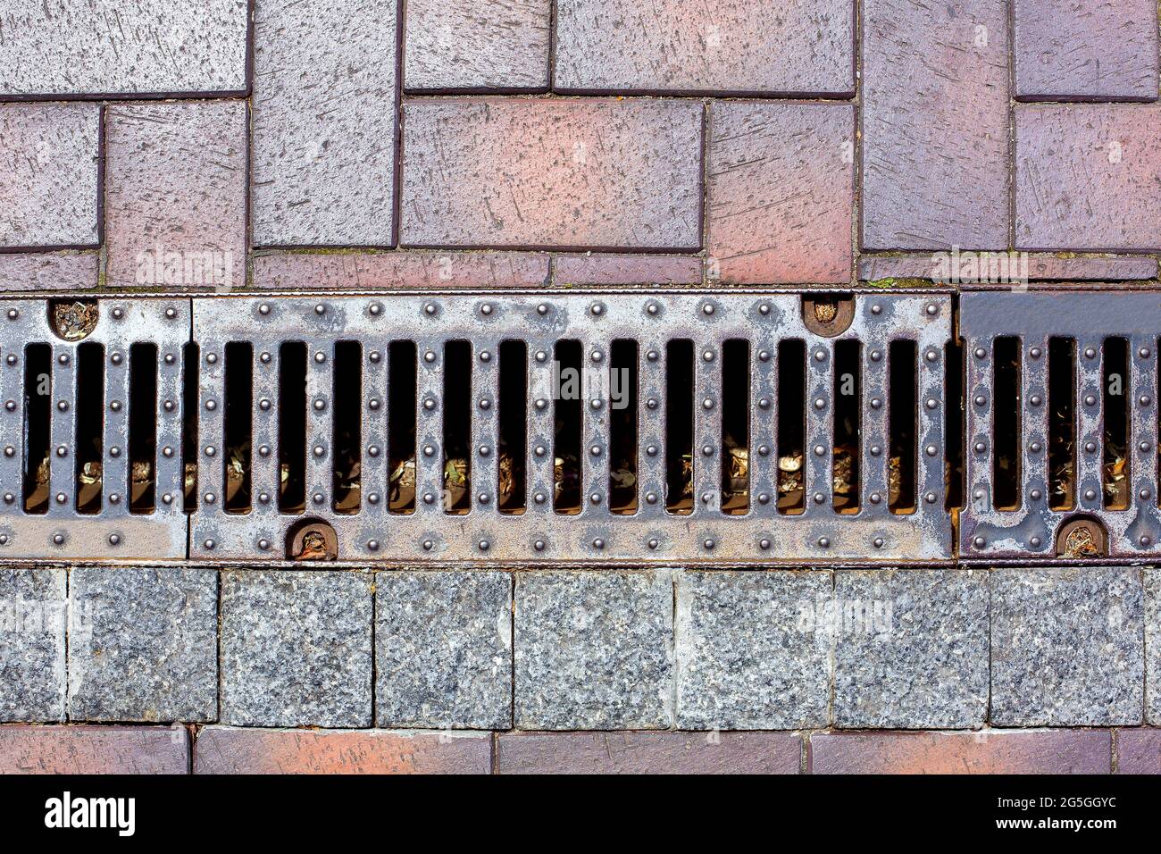 an iron drainage grate of a rain channel on a pedestrian sidewalk made ...