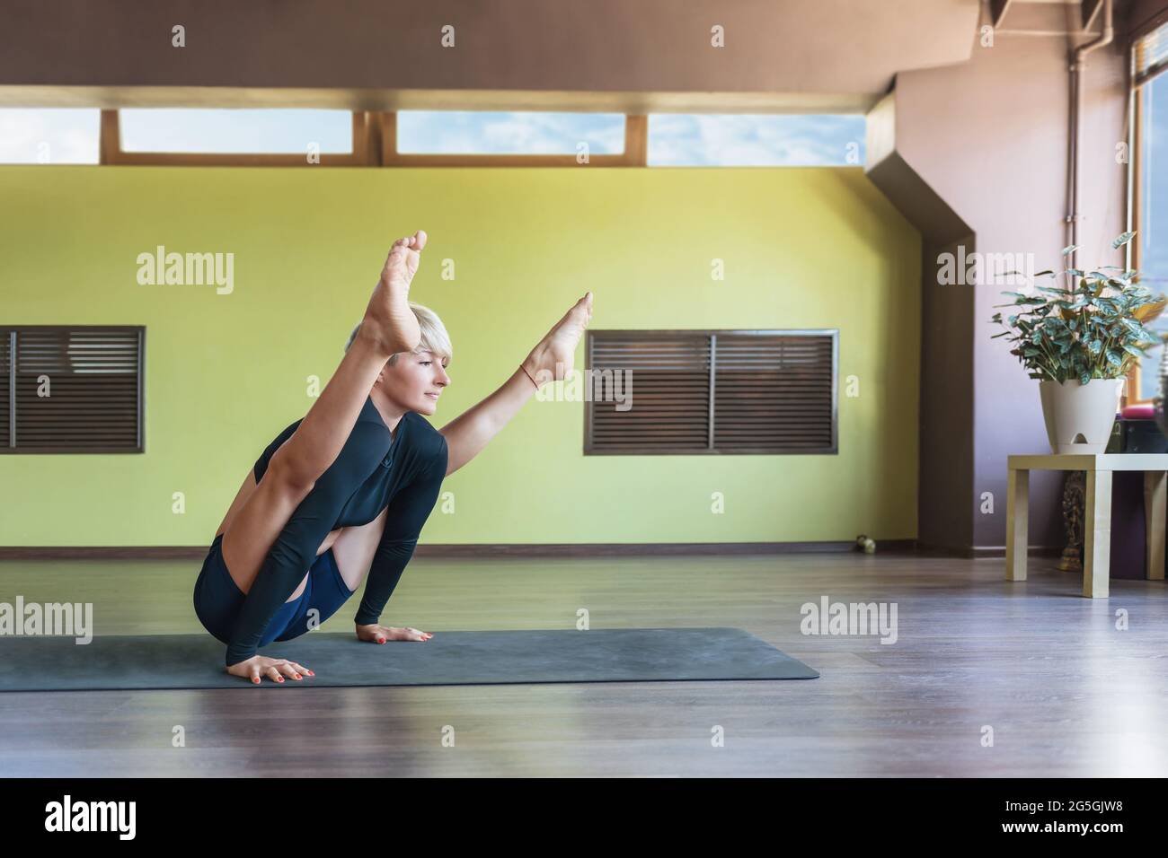 Blonde woman practicing yoga, performs in the gym exercise tittibhasana ...