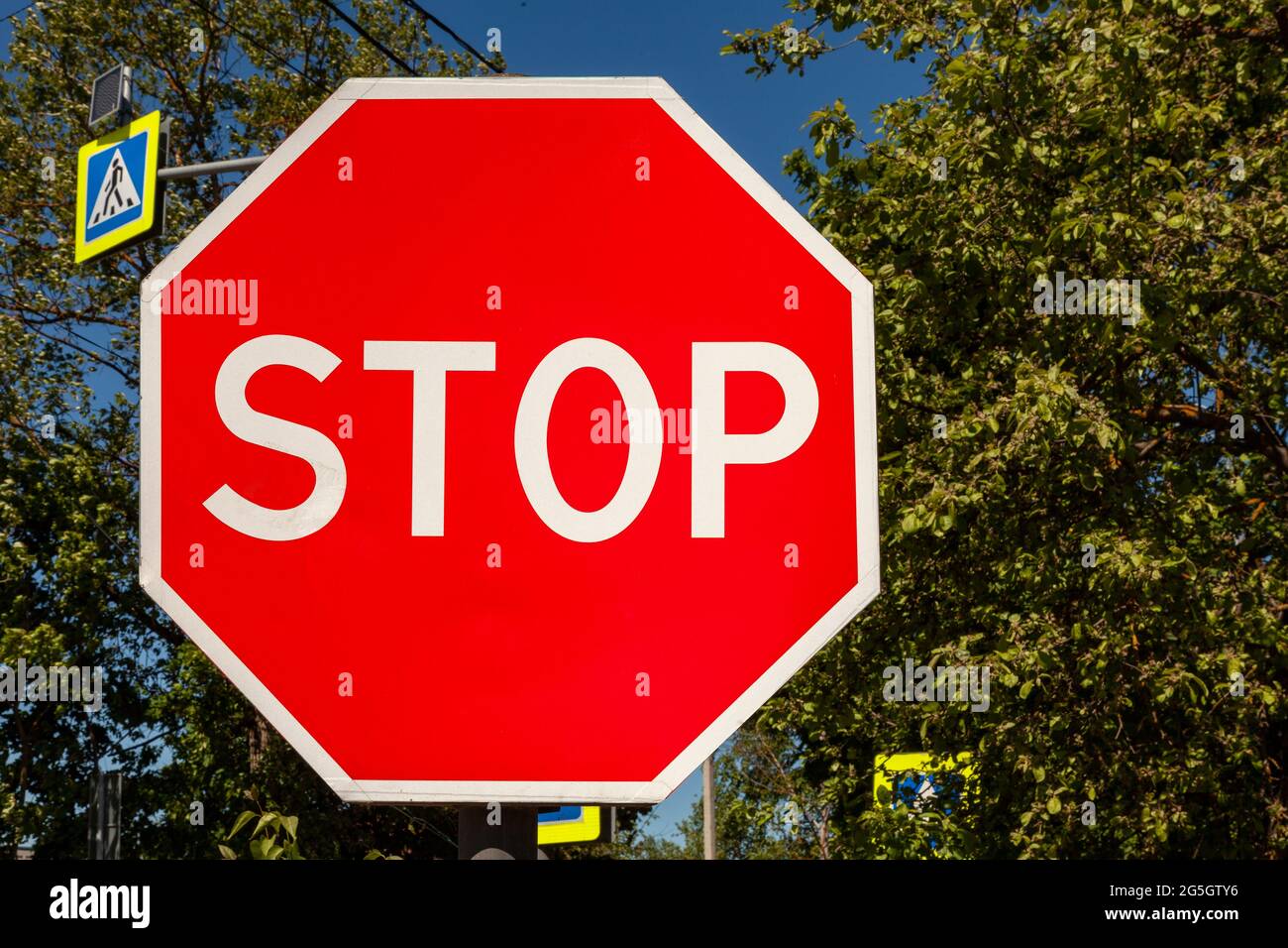 Large road sign Stop against the background of green trees and blue sky ...