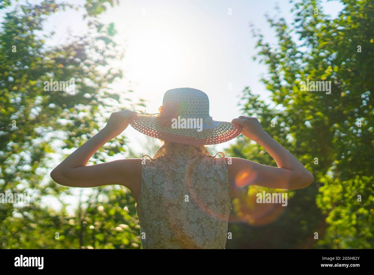 back view of adult woman in summer hat raise hands to the sun shine ...