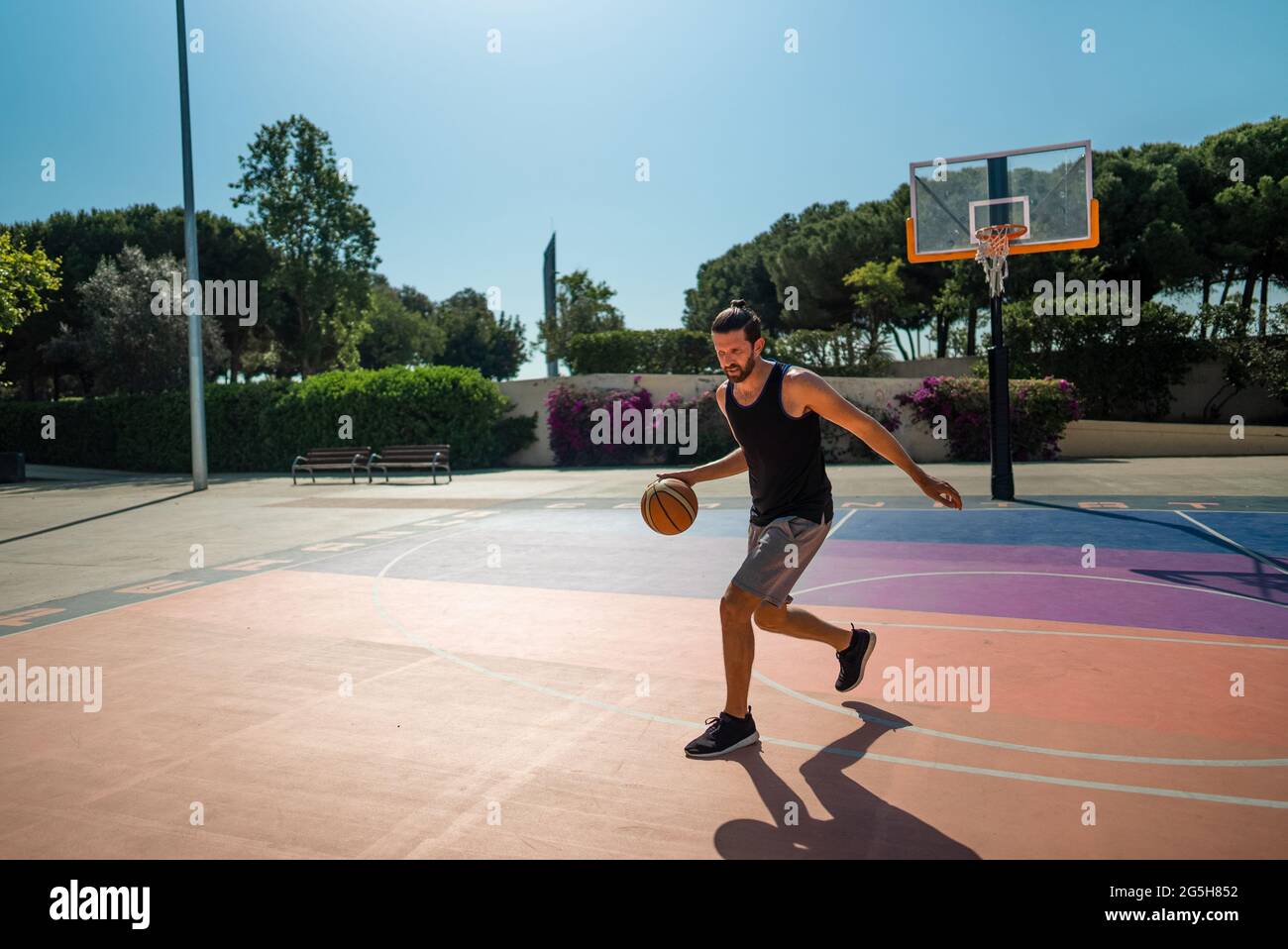 A male basketball player trains himself on a basketball court with a ...