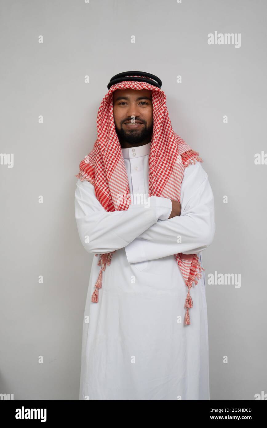 an arabian young man in a turban standing smiling with crossed hands ...