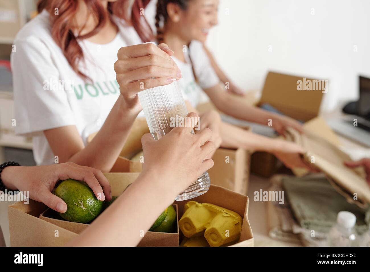 Hands of volunteers of charity center putting groceries, water and ...