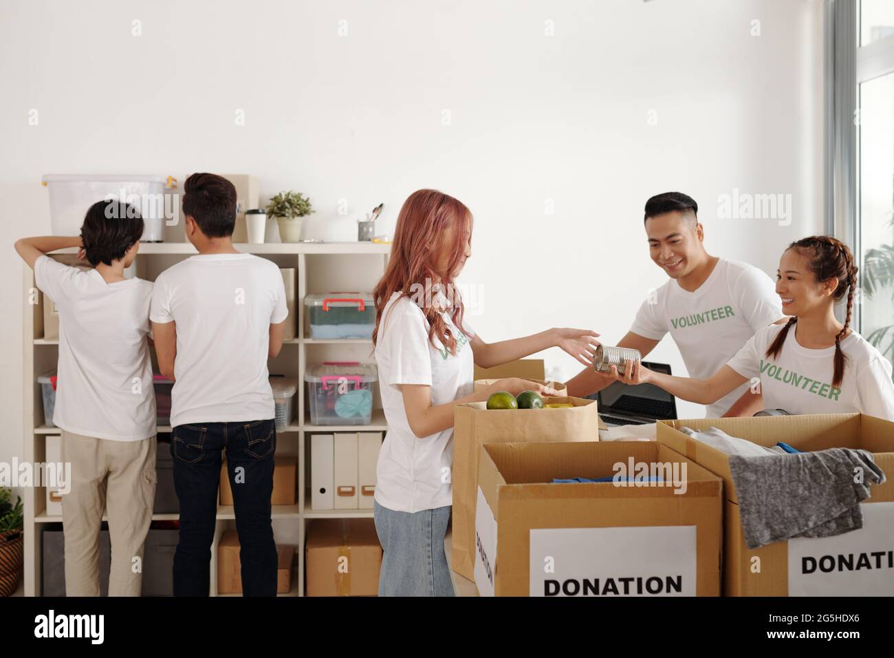 Group of young people working in community donation center, unpacking ...