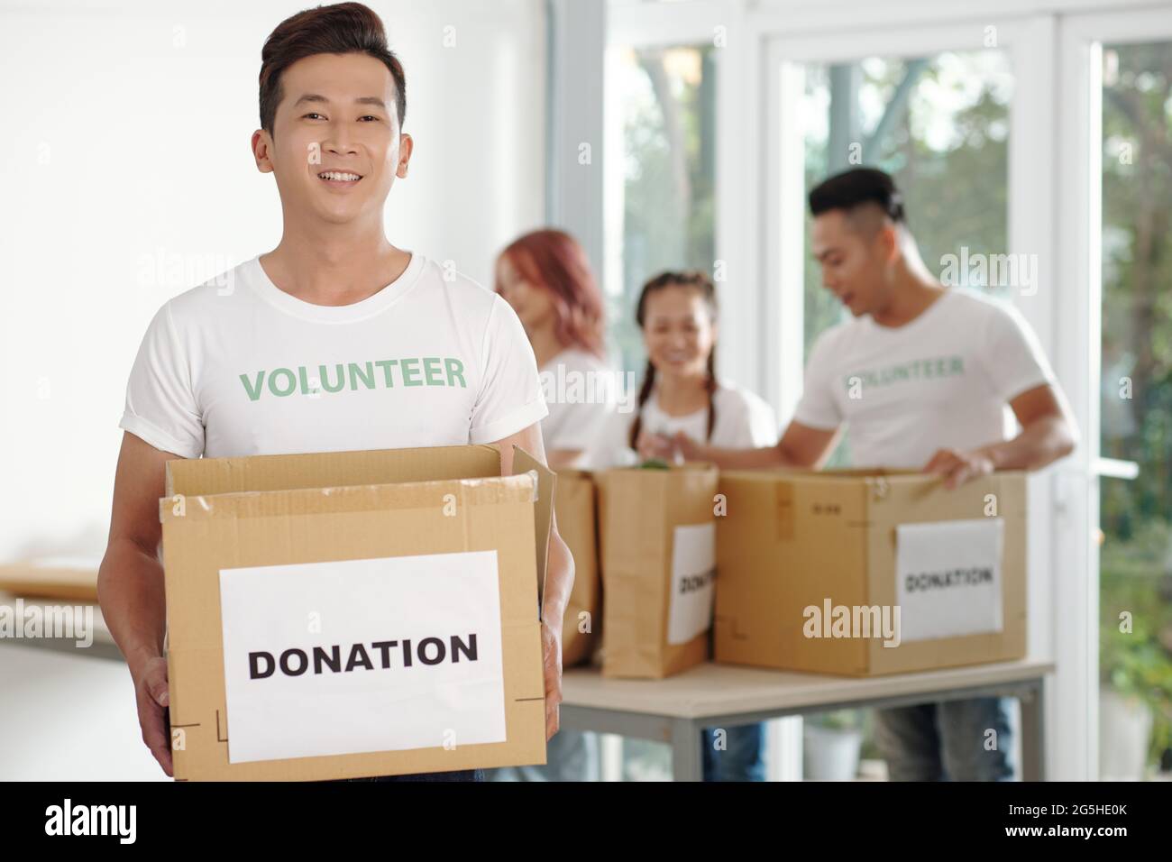 Positive handsome young man enjoying working at community donation ...
