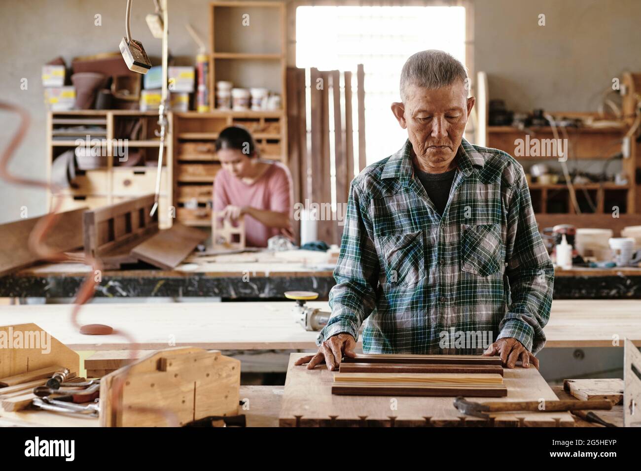 Serious pensive senior carpenter looking at pieces of walnut and maple ...