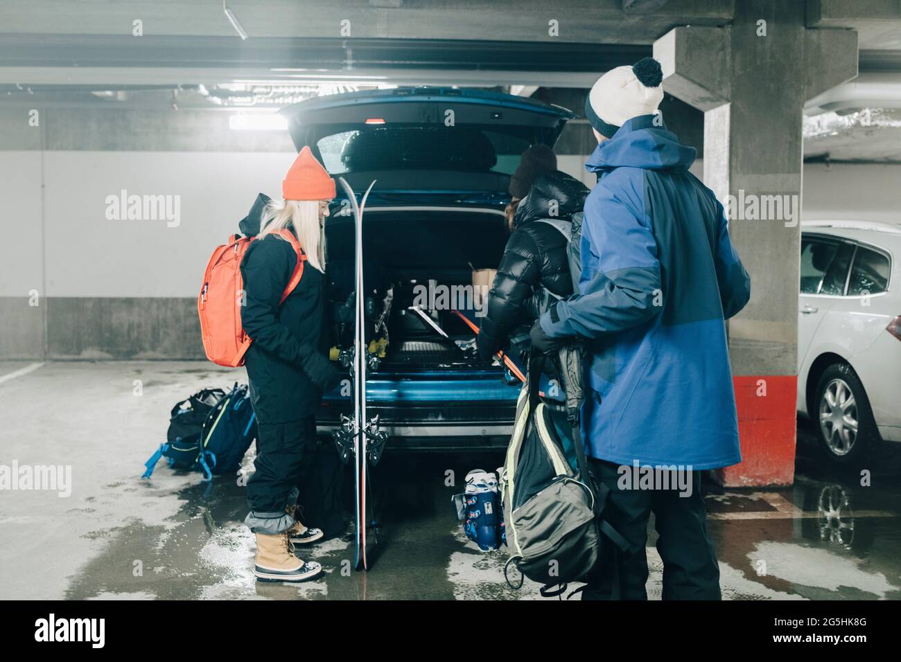 Male and female friends loading luggage in car trunk at parking garage ...