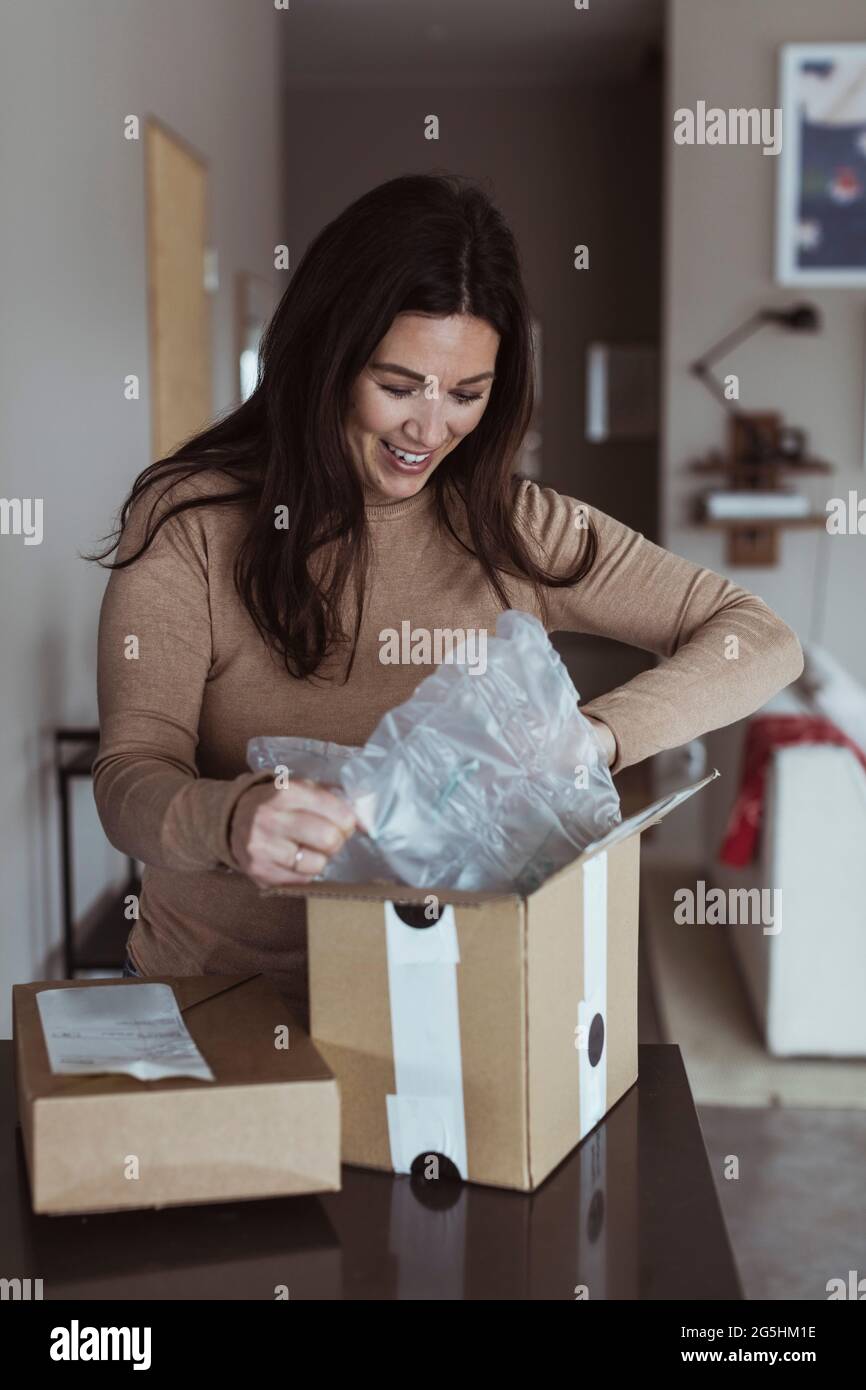 Excited woman opening box package on side table in living room Stock ...