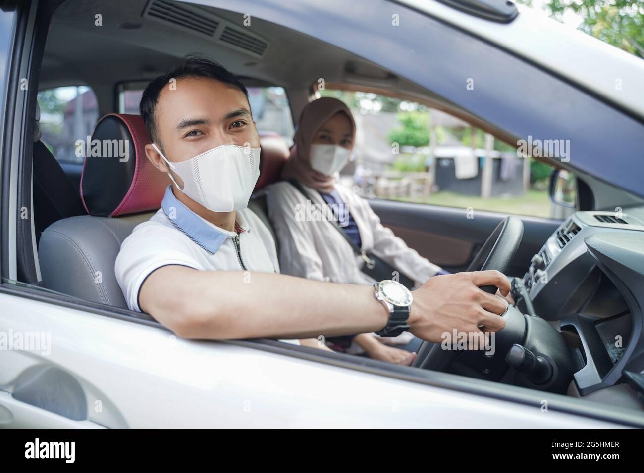 a young asian man in a mask looks at the camera while driving in a car ...