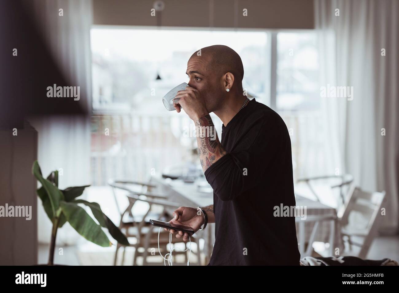Hispanic man drinking coffee while standing in living room Stock Photo ...