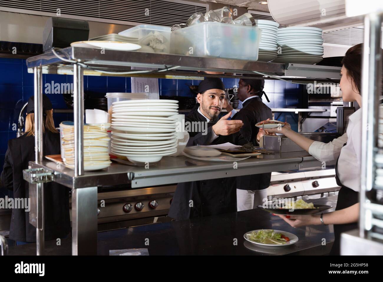 Woman waiter is giving order to chef cook on kitchen in restaurant ...