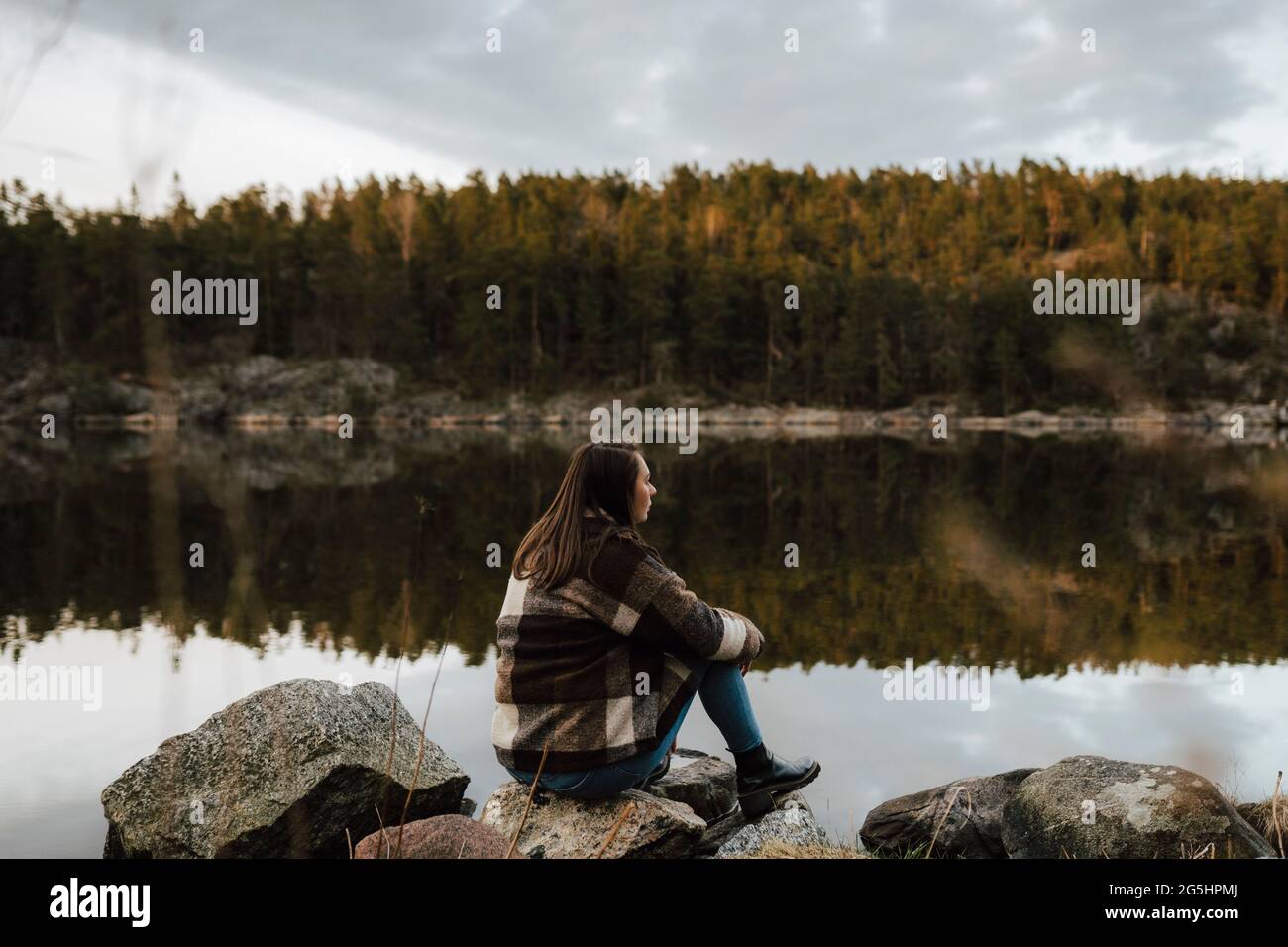 Young female explorer admiring lake while sitting on rock during ...