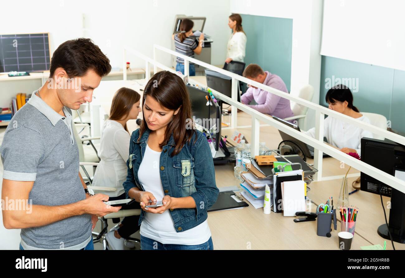 Friendly male and female colleagues exchanging phone numbers in modern ...