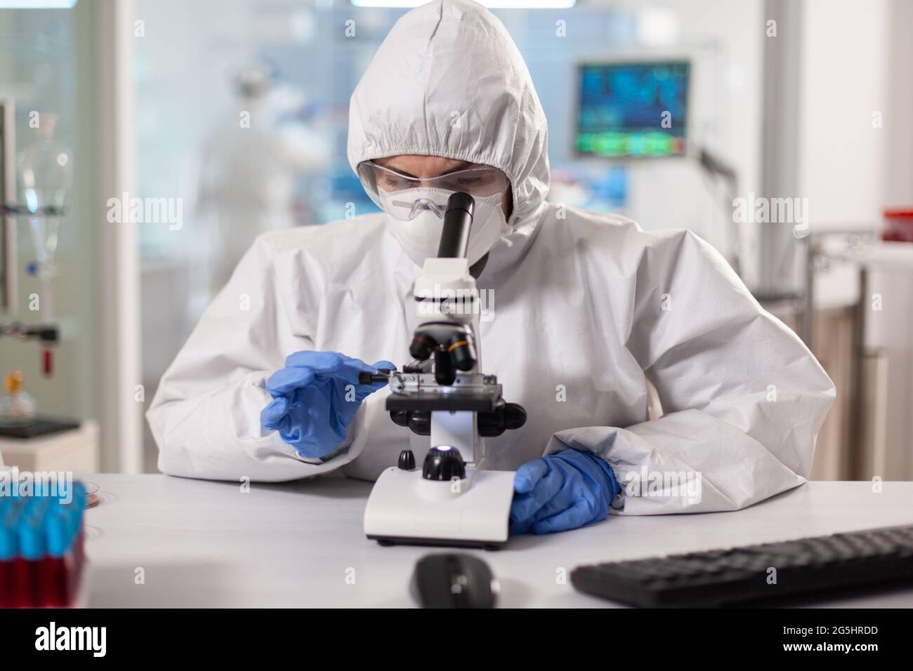 Scientist in ppe suit making adjustments and looking through laboratory ...