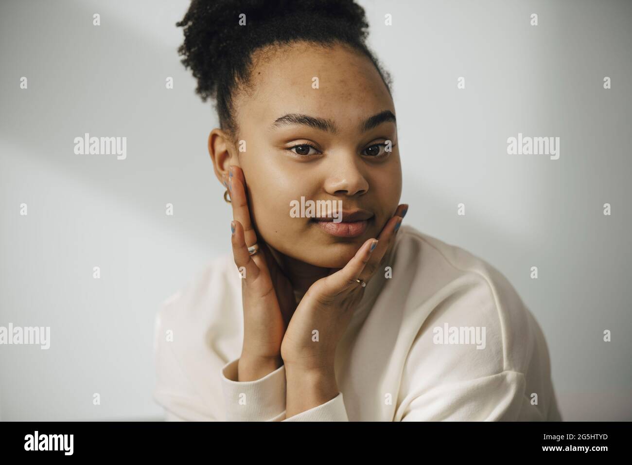 Young woman with hand on chin against white wall Stock Photo - Alamy