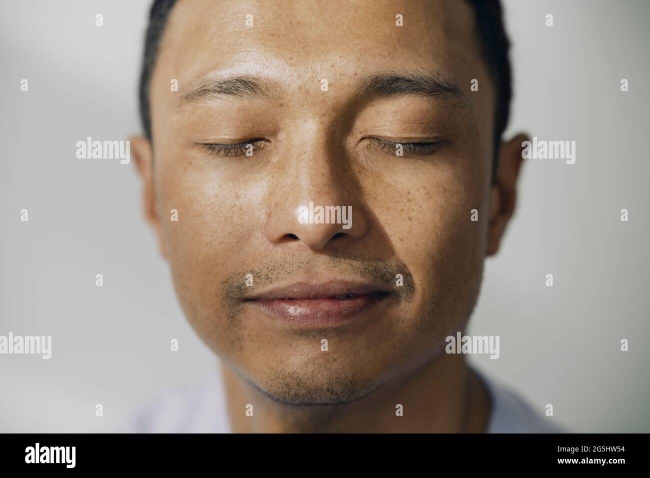 Smiling man with eyes closed against white wall Stock Photo - Alamy
