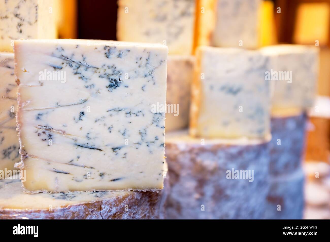 Stacks of whole and cut Stilton cheeses for sale at a market. This is a ...