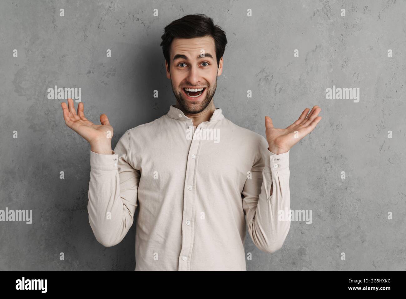 Excited handsome unshaven guy posing with hands up isolated over grey ...