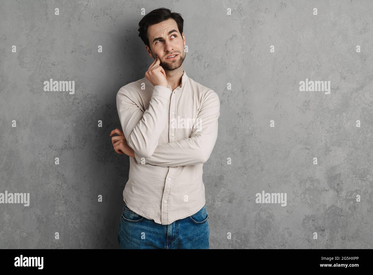 Brooding handsome guy thinking and looking upward isolated over grey ...