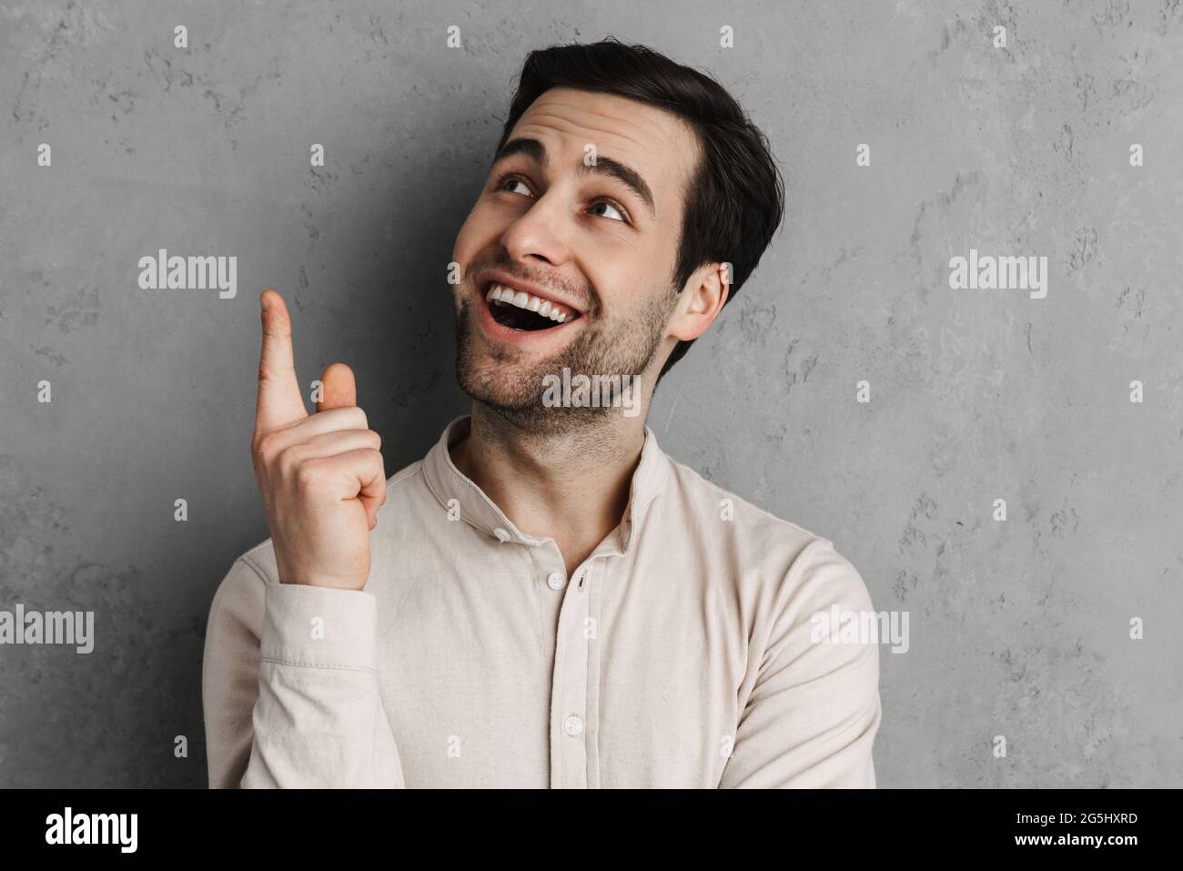 Joyful handsome guy smiling and pointing finger upward isolated over ...