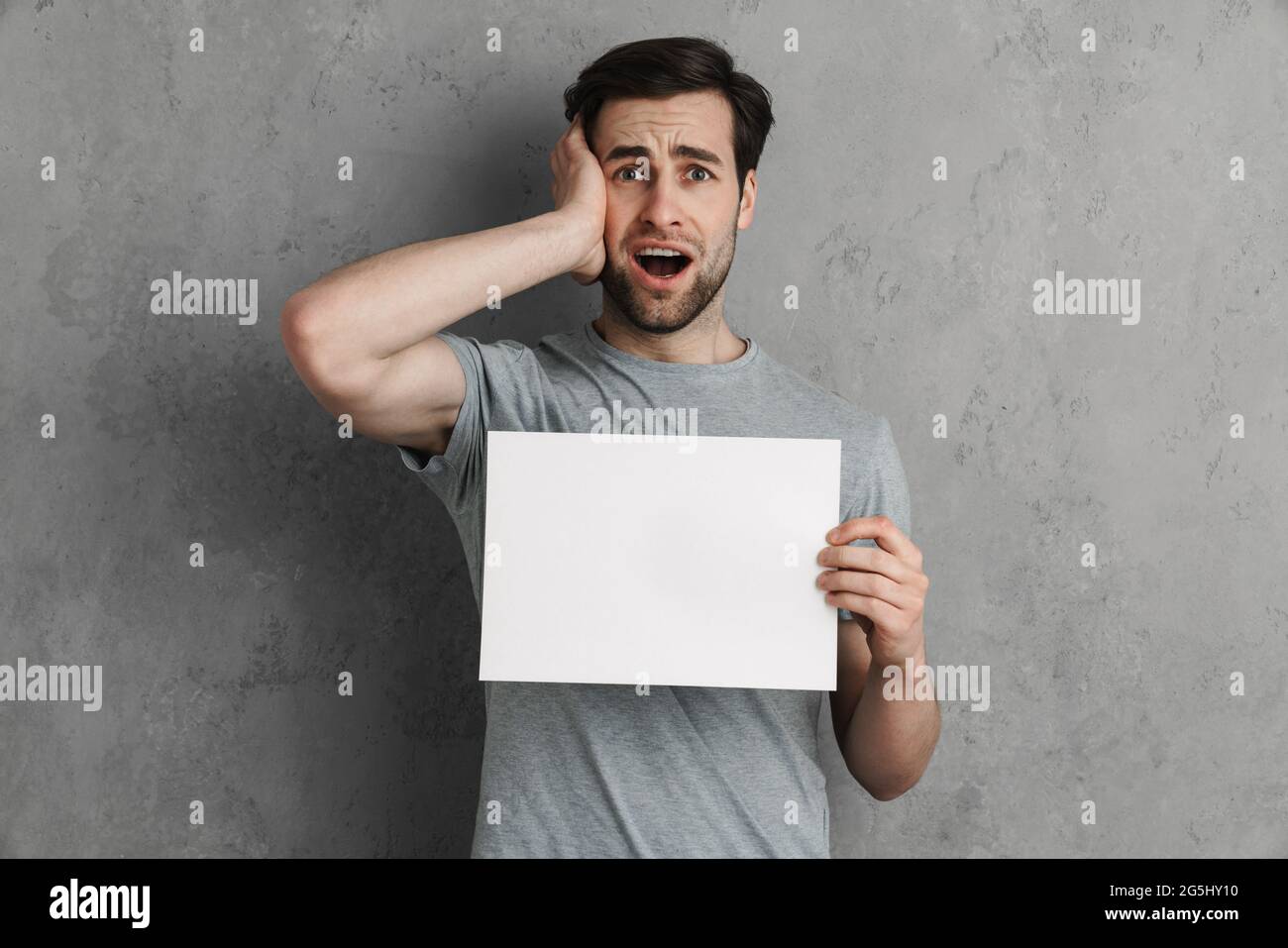 Shocked handsome casual man showing blank board isolated over gray ...