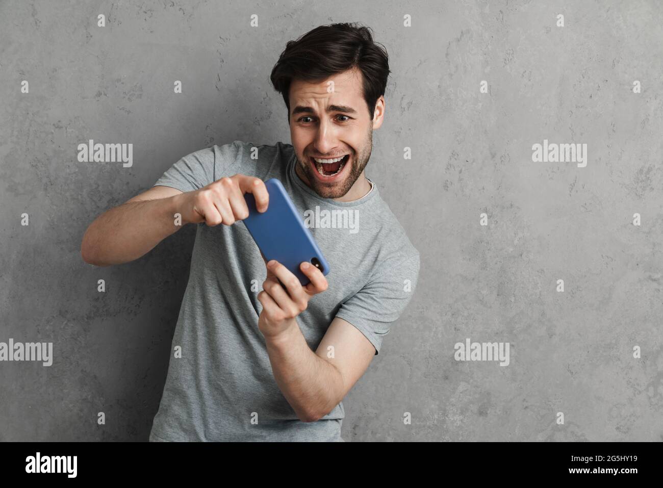 Stressed handsome guy screaming while playing online game on cellphone ...