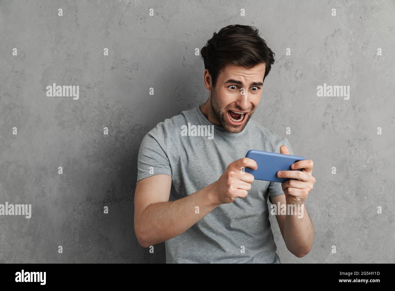Stressed handsome guy screaming while playing online game on cellphone ...