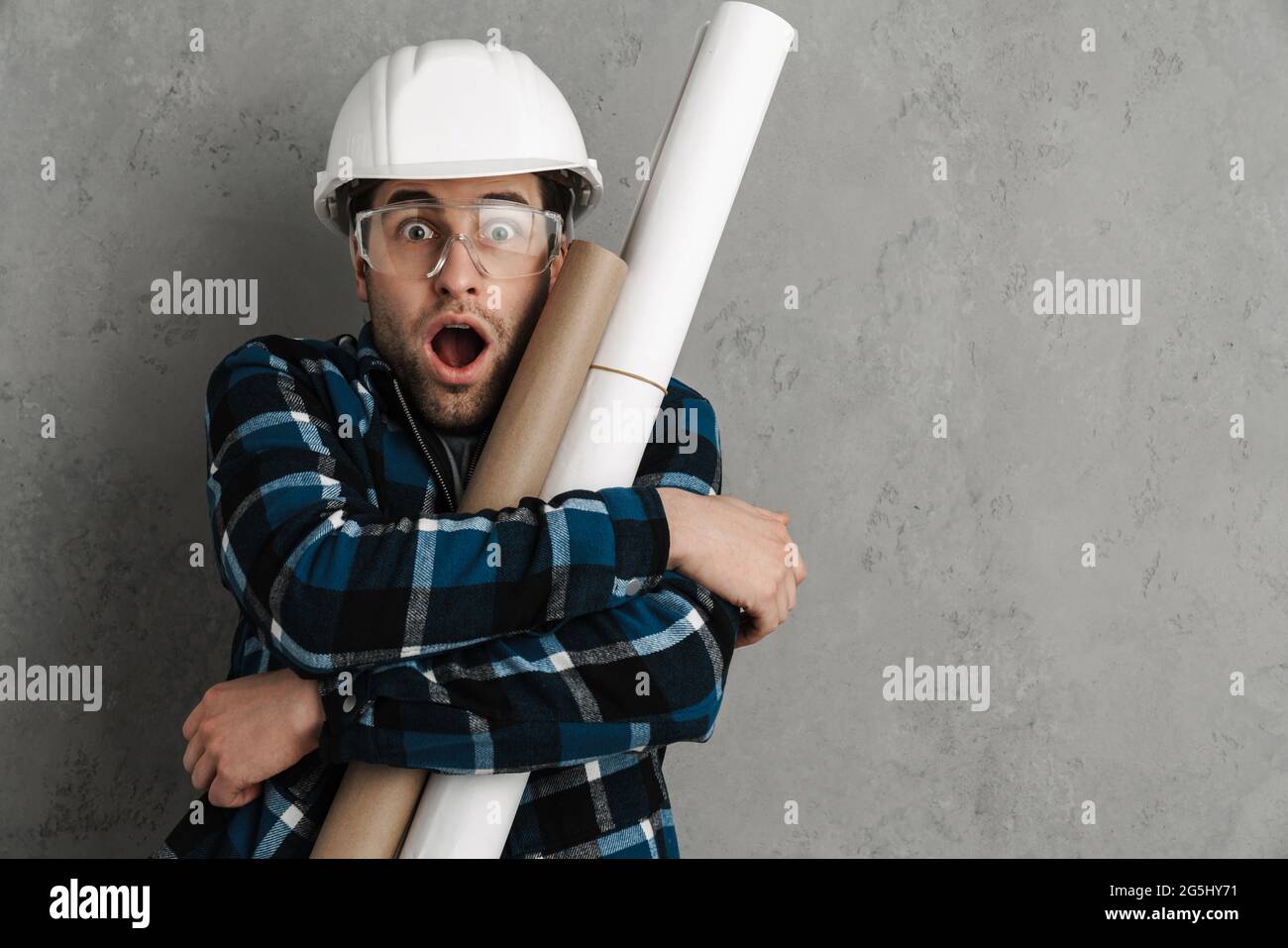 Young shocked handsome civil engineer in hardhat holding blueprints ...