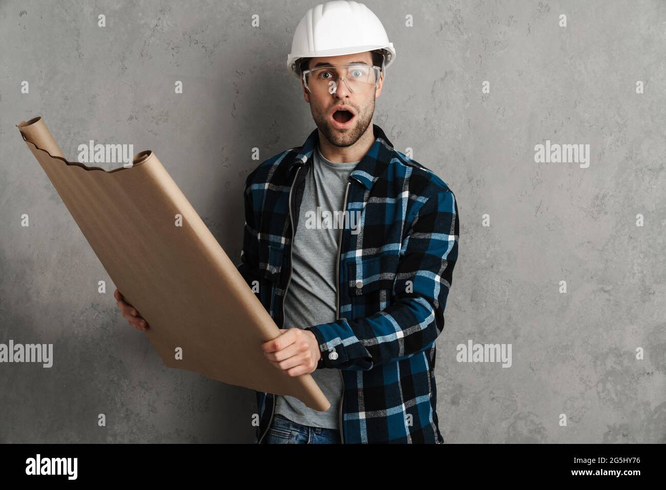 Young shocked handsome civil engineer in hardhat holding blueprints ...