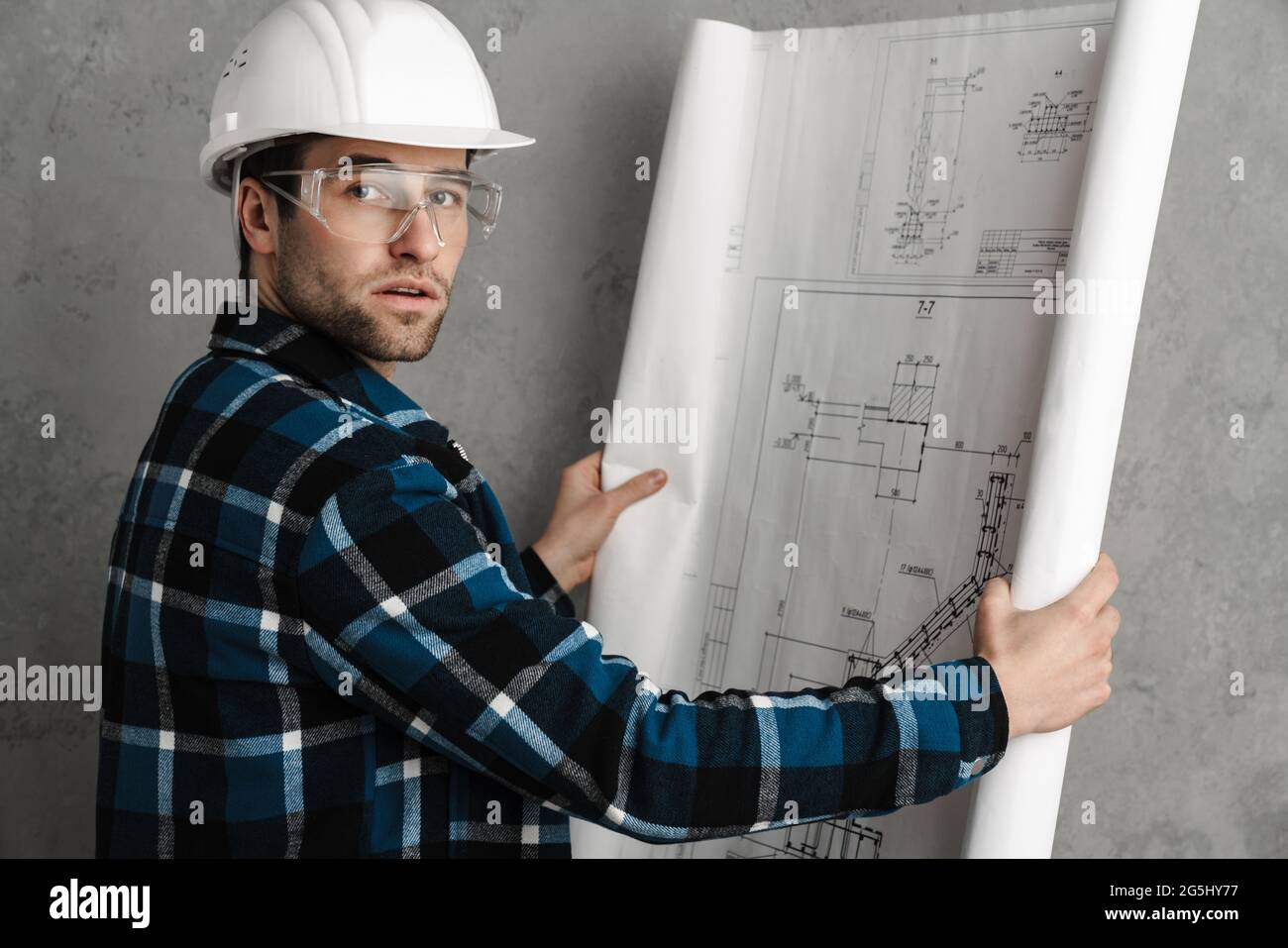 Young handsome civil engineer in hardhat holding blueprints standing ...