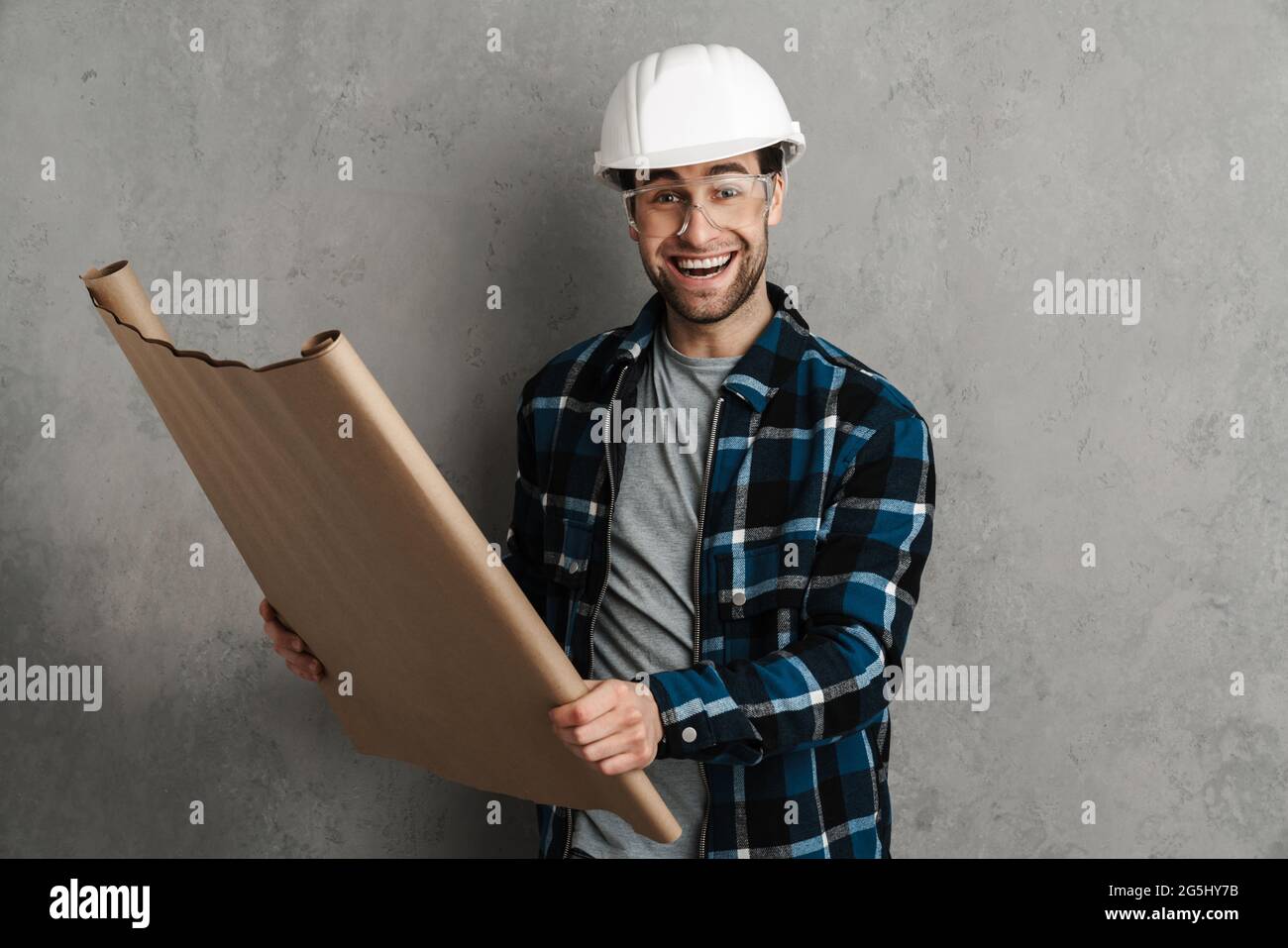 Young happy handsome civil engineer in hardhat holding blueprints ...