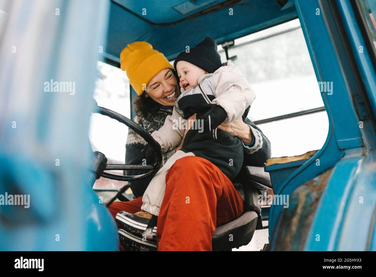 Cheerful mother with daughter sitting in tractor during winter Stock ...