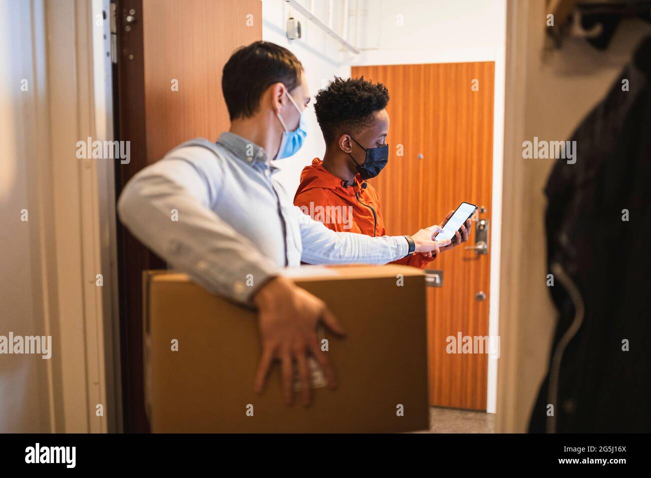 Male customer receiving parcel from young delivery man during COVID-19 ...