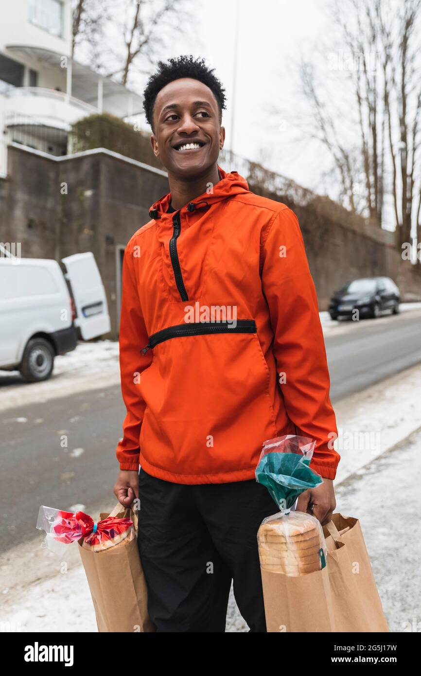 Happy young delivery man carrying paper bags while walking on road ...