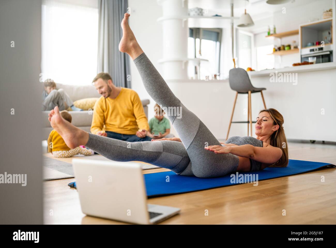 Young woman, mother exercising at home in living room, father playing ...