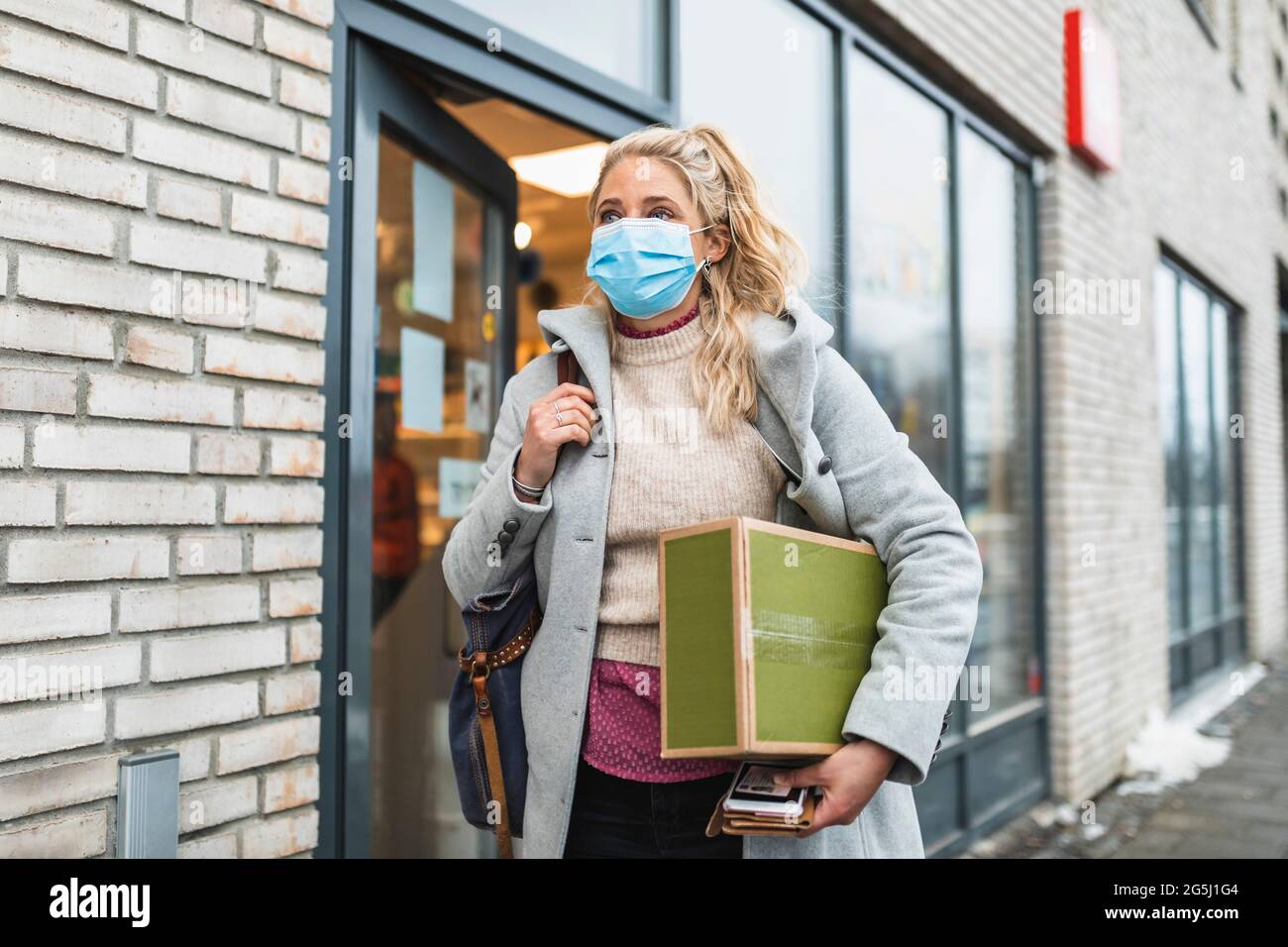 Blond female customer carrying package outside retail store during ...