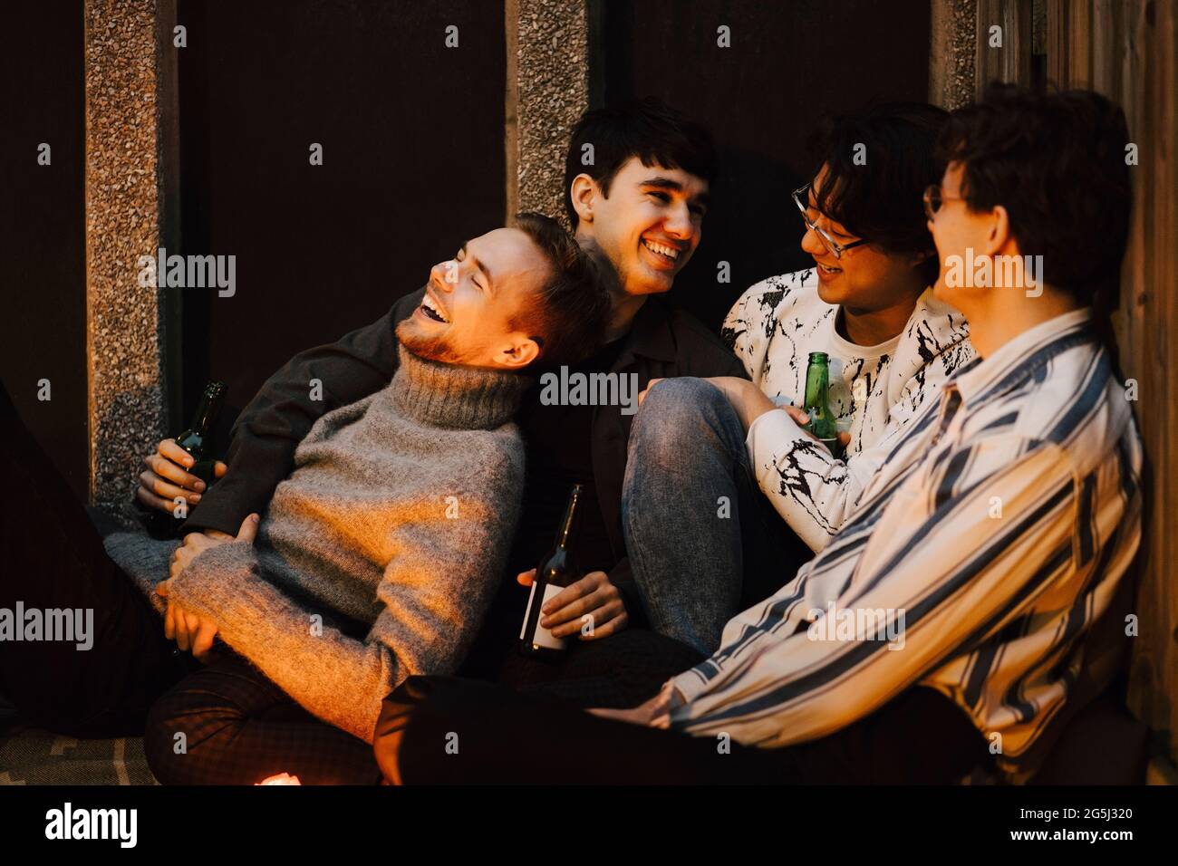 Happy male friends chilling with beer bottles while sitting at balcony ...