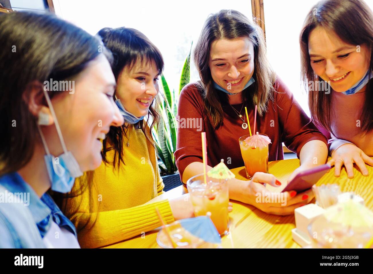 Girls friends look at a mobile phone and smile - Millennials in a cafe ...