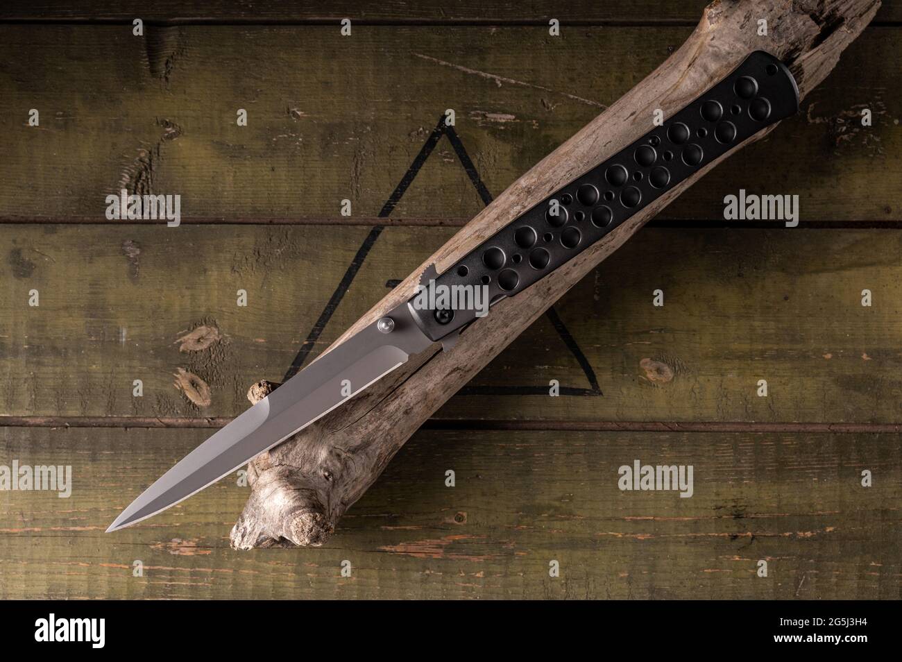 A large folding knife on a tree. Knife on an old dry branch. Sharp long ...